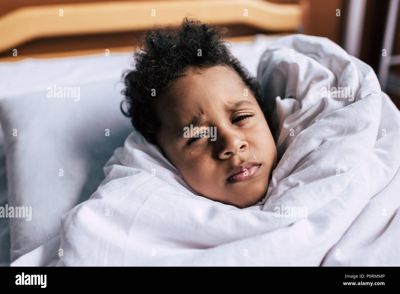portrait of sick african american little boy covered in blanket lying ...