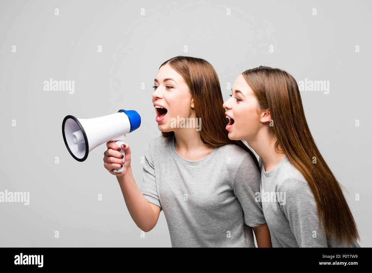 side view of young twins screaming into loudspeaker in hands isolated ...