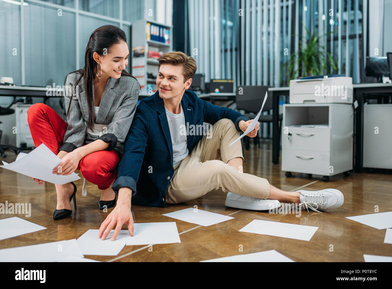 young happy business partners doing paperwork while sitting on floor at ...