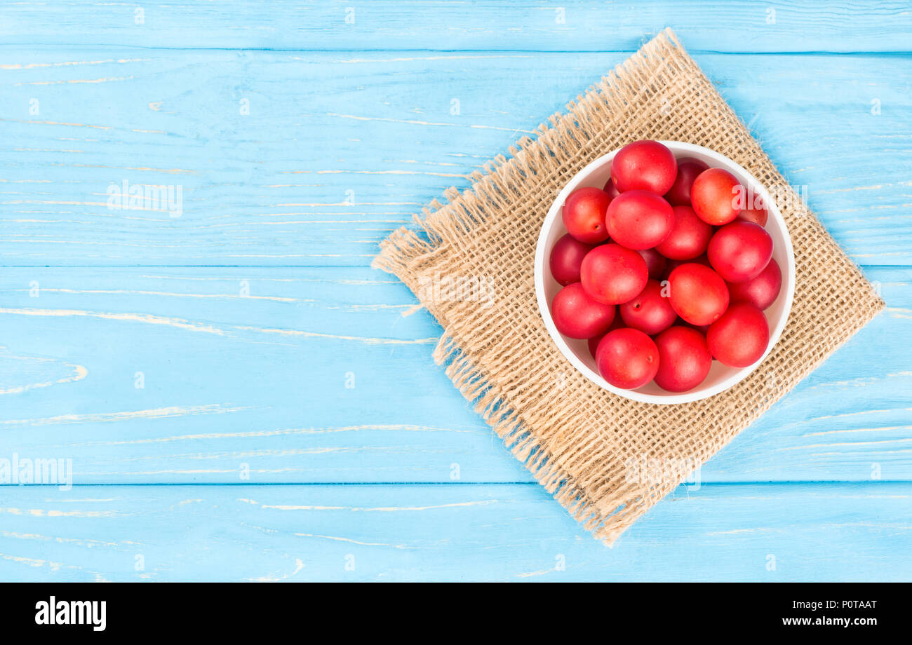 Fresh red cherry plum in a bowl on sacking and blank wooden background ...