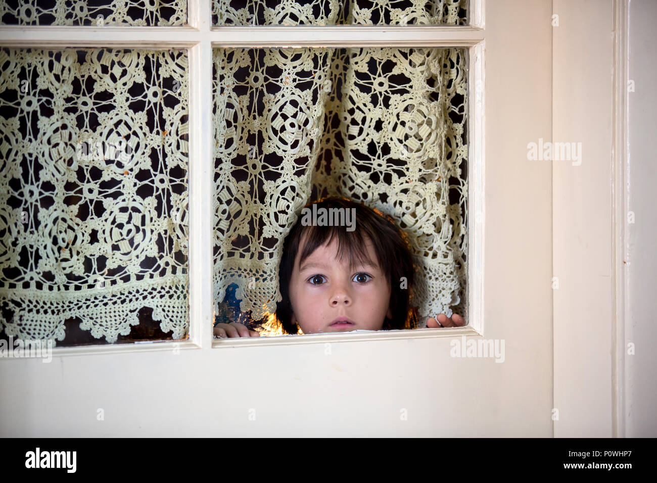 Little preschool boy, child, looking out scared through a door with ...
