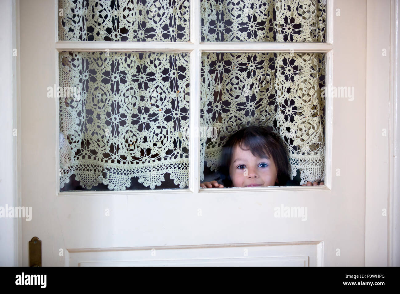 Little preschool boy, child, looking out scared through a door with ...