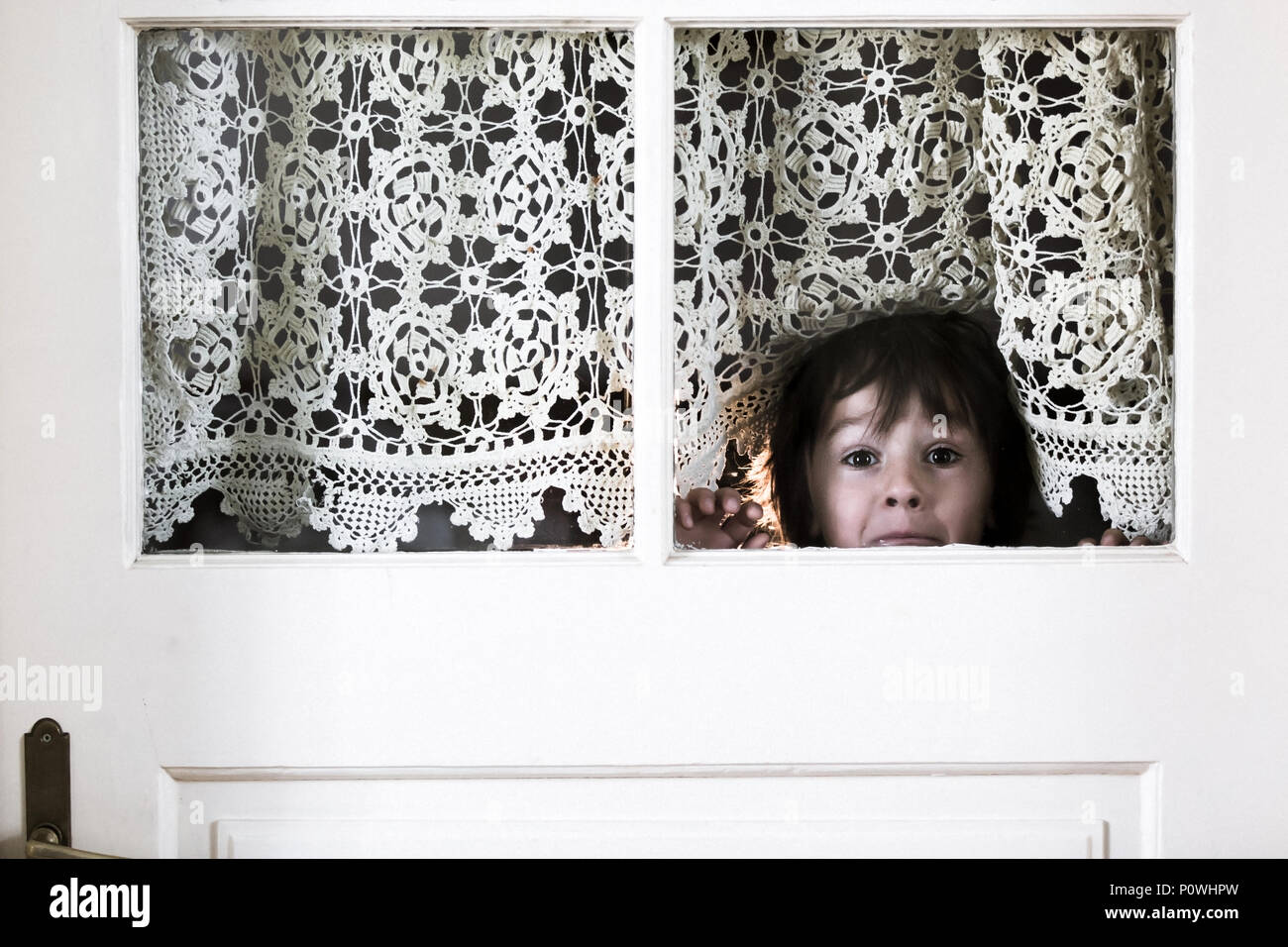 Little preschool boy, child, looking out scared through a door with ...