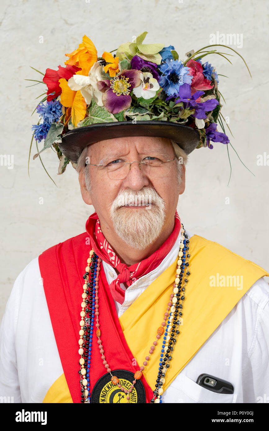 A morris dancer wearing a hat covered in summer flowers and wearing a ...