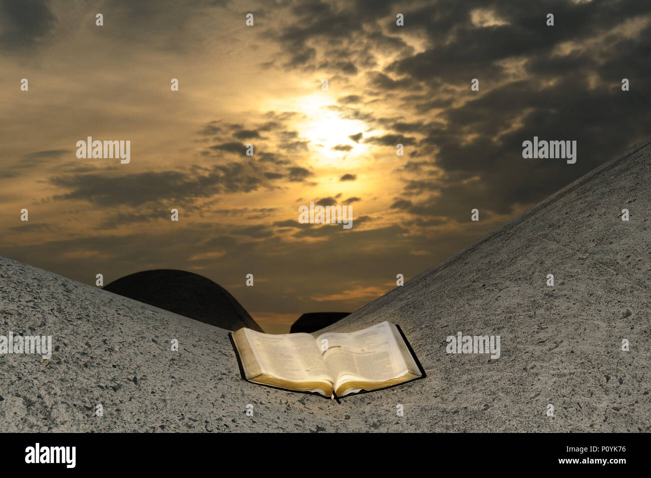 Bible open upon a breakwater block in front of a stunning orange sky at ...