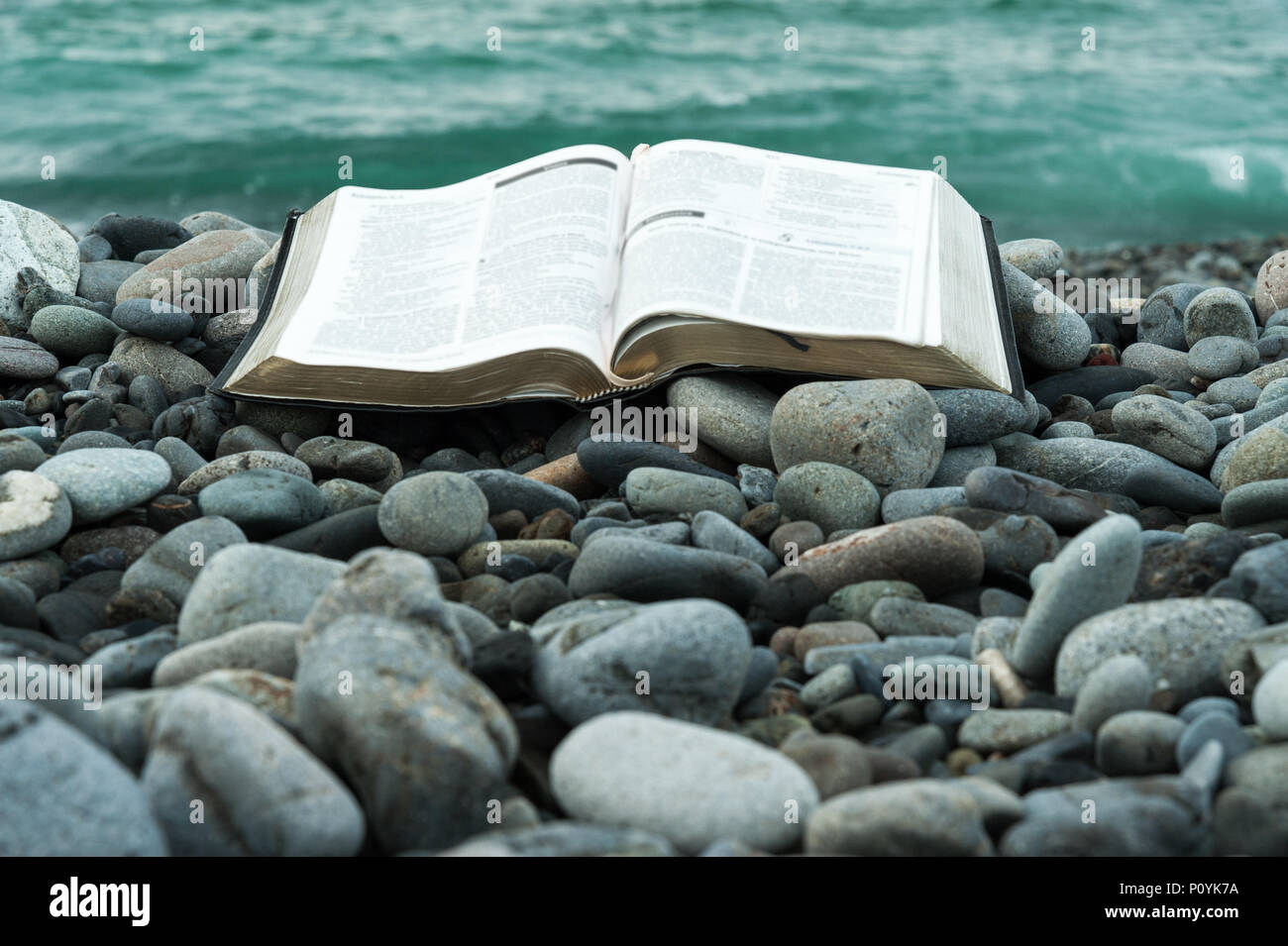 Bible open on top of small stones in front of the green sea. Copy space ...
