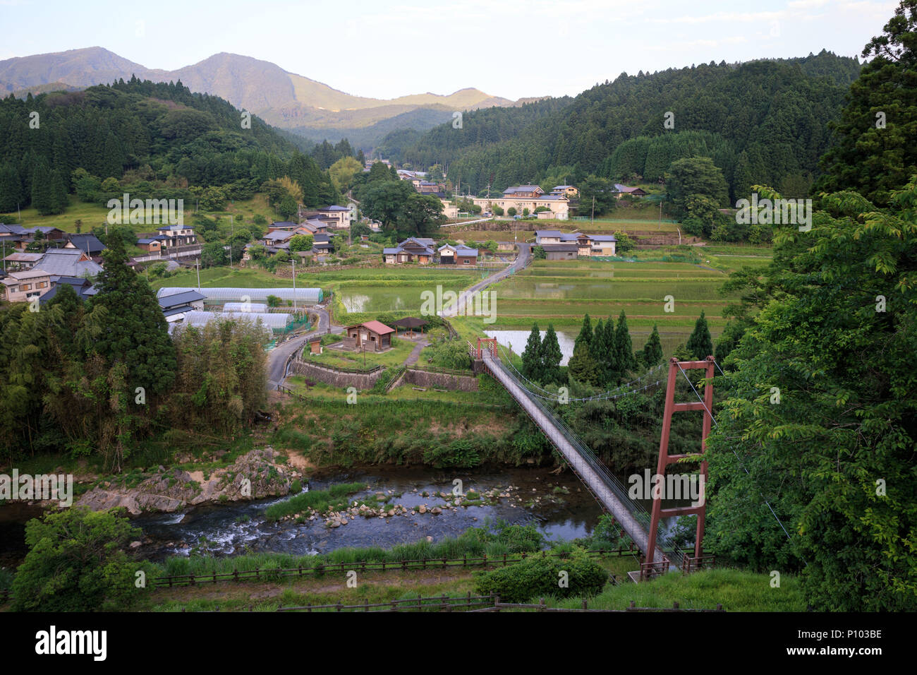 Small red suspension footbridge across river to rural Japanese farming ...