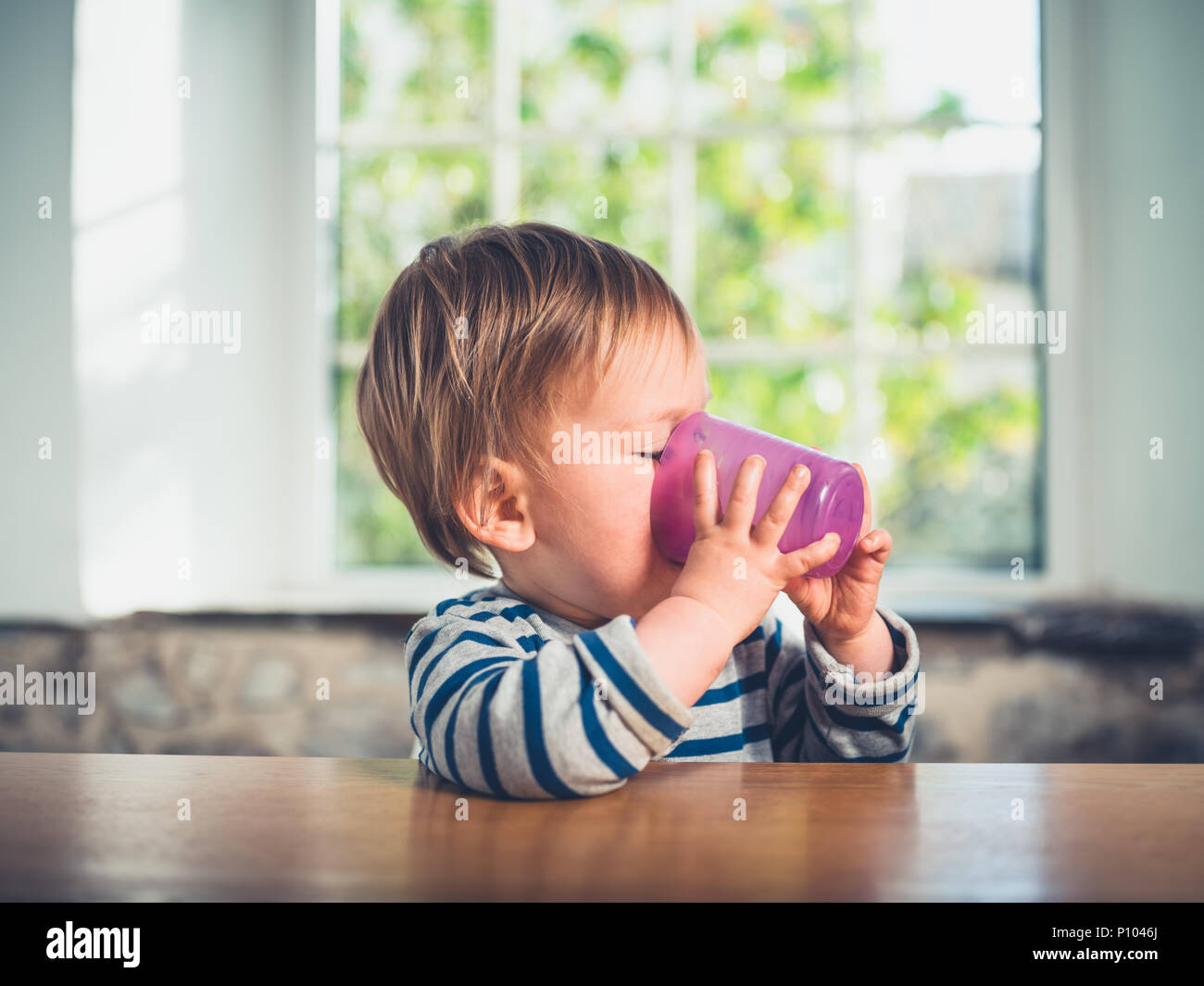 A cute little boy is sitting at the table drinking from a cup Stock ...