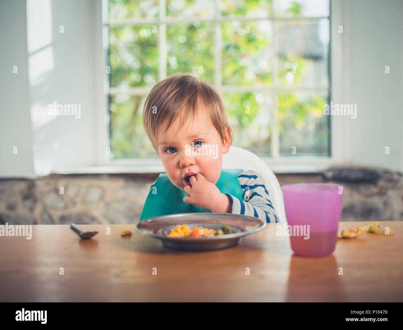 A cute little boy is sitting at the table and is eating his dinner ...