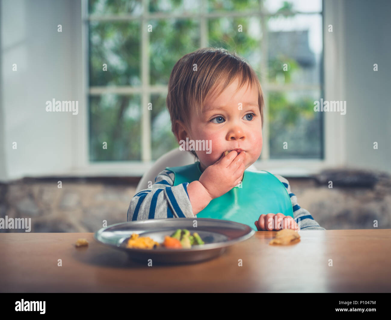 A cute little boy is sitting at the table and is eating his dinner ...