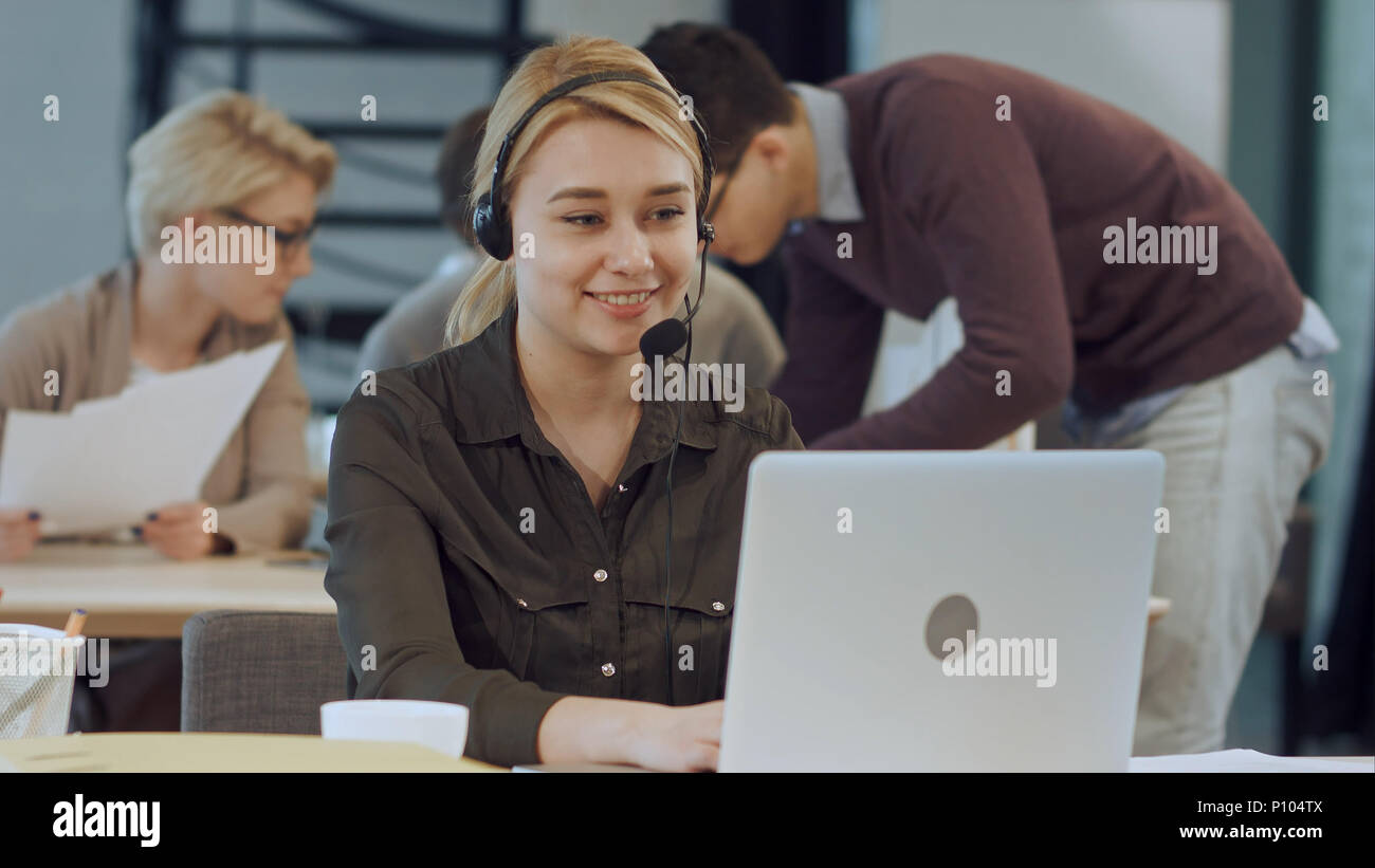 Smiling female helpline operator with headphones at her desk in the ...