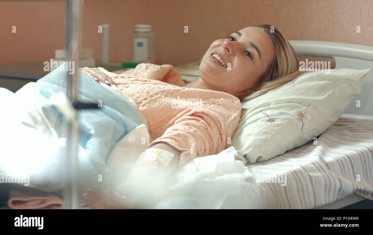 Young female patient lying in hospital bed on drip talking to a doctor ...