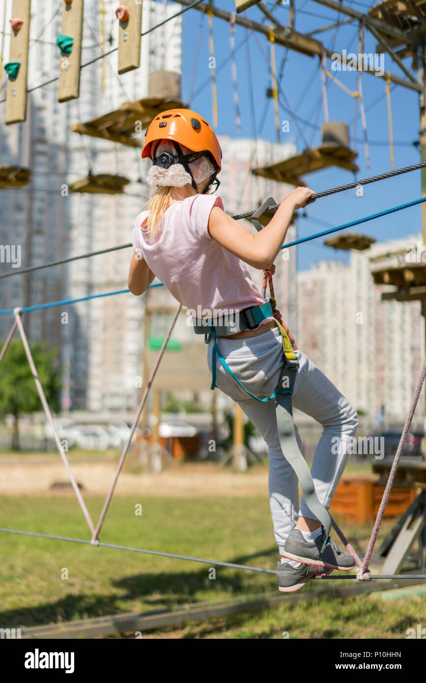 Little beautiful girl climbs on rope harness in summer city park Stock ...