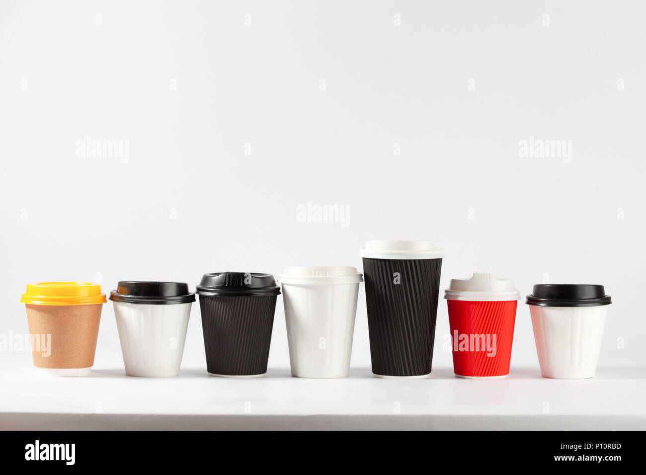 Disposable coffe cups different colors and sizes in a row on white ...