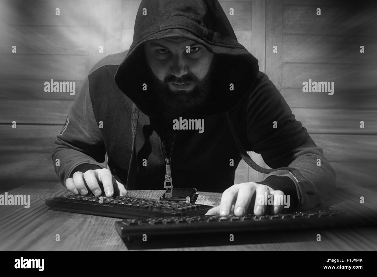 A bearded man in a hood sits and works behind a computer hacker Stock ...