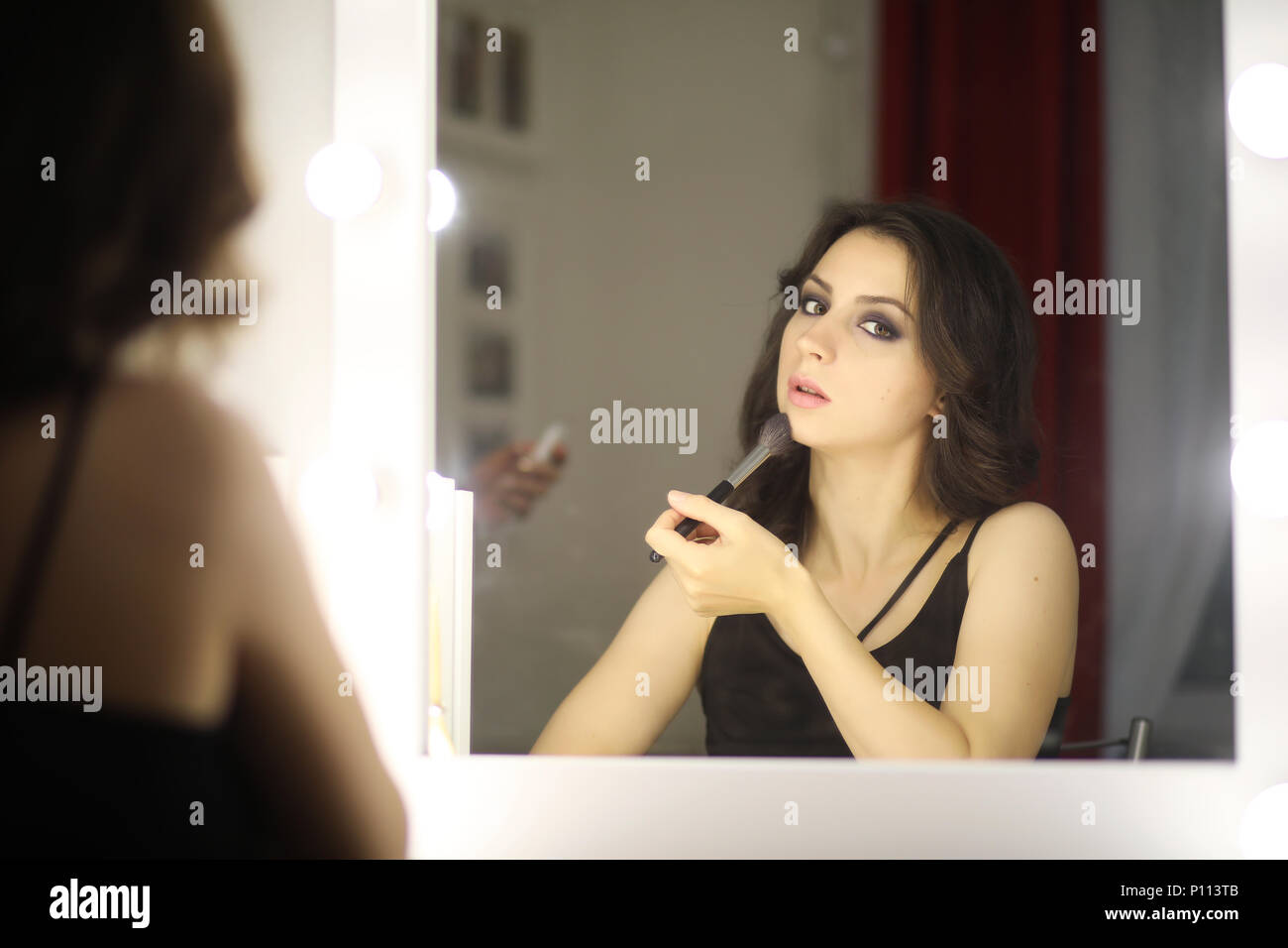 Beautiful girl doing makeup in front of a mirror Stock Photo - Alamy