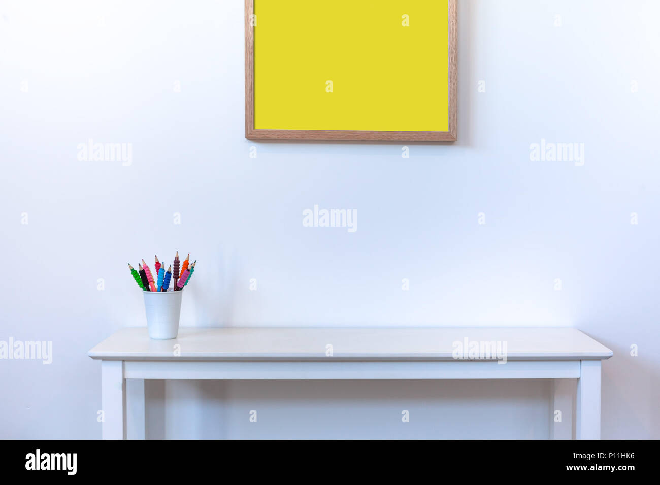 Empty picture frame above side table with colorful pencils in cup ...