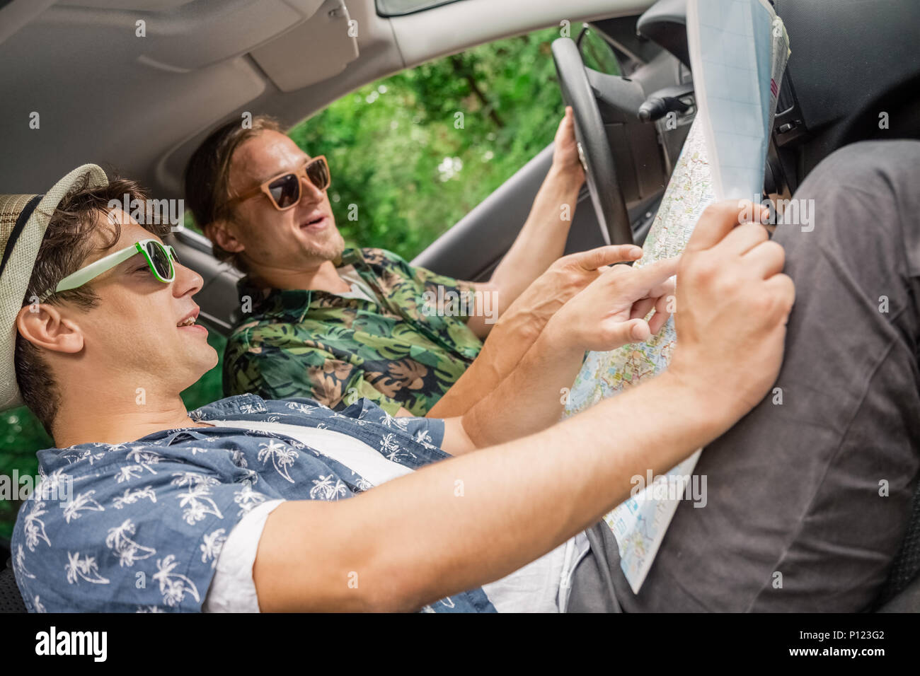 Modern fashionable guys driving a car and looking at road map. Roadtrip ...