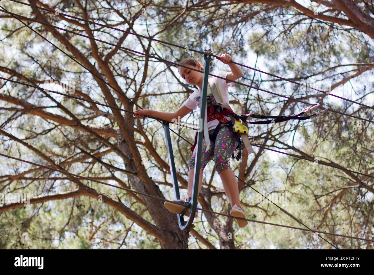 Girl teenager with frightened face with climbing equipment in the rope ...