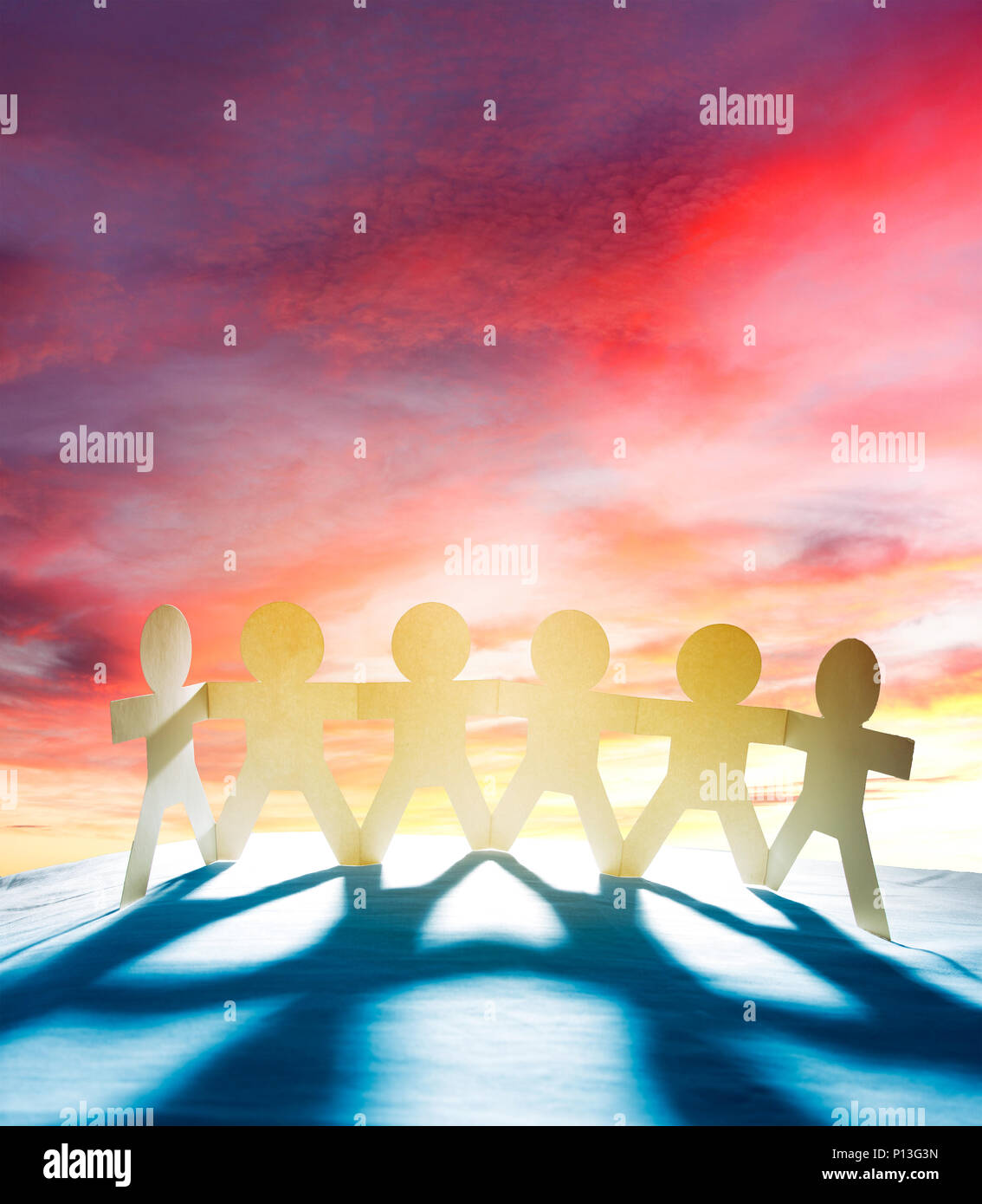 Team of six paper chain people holding hands in front of bright sky ...