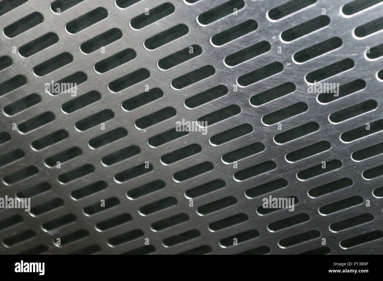 stainless steel grating with oblong holes on black background, close-up ...