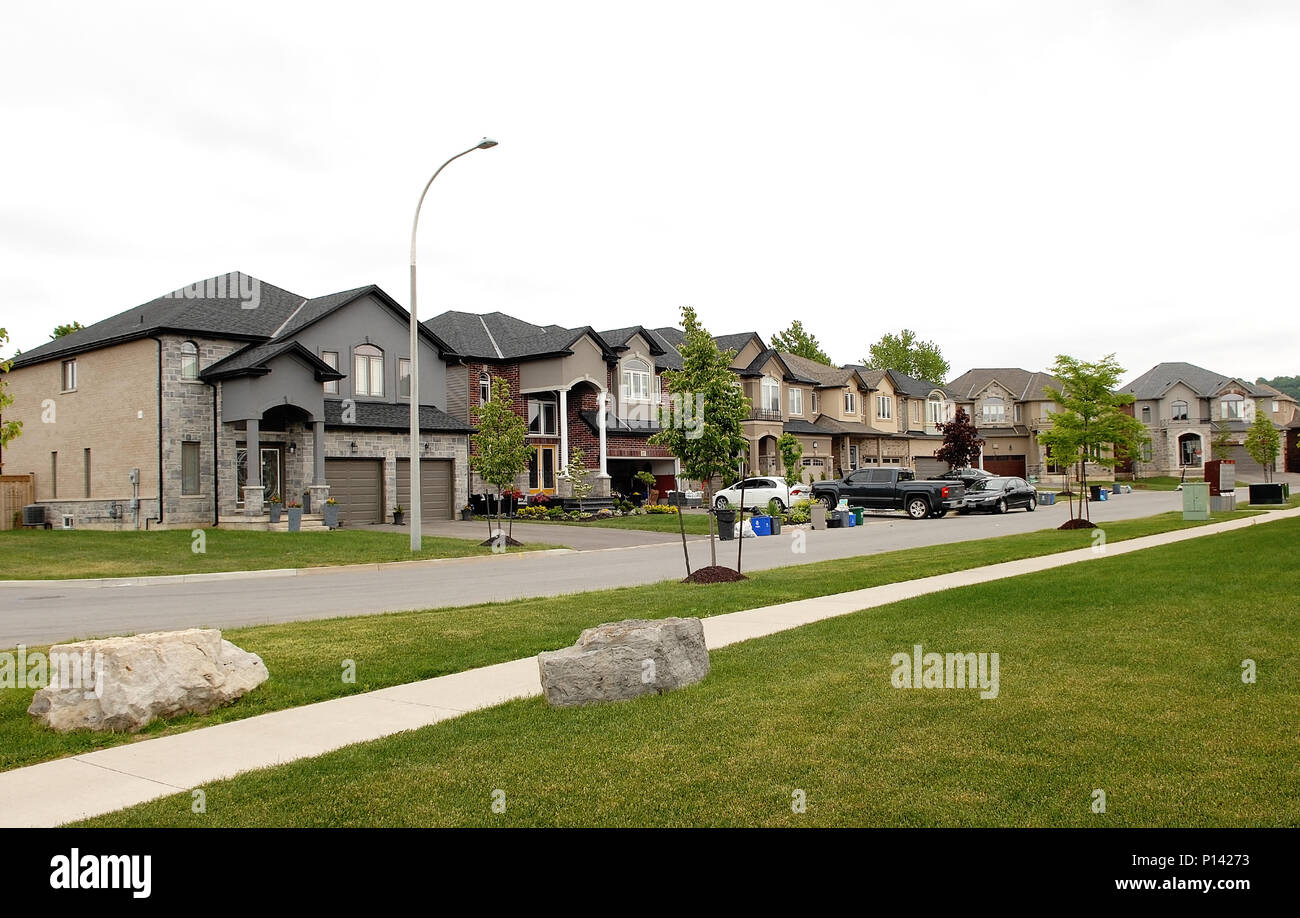 A suburban street with new big houses in the summer time whit cars in ...