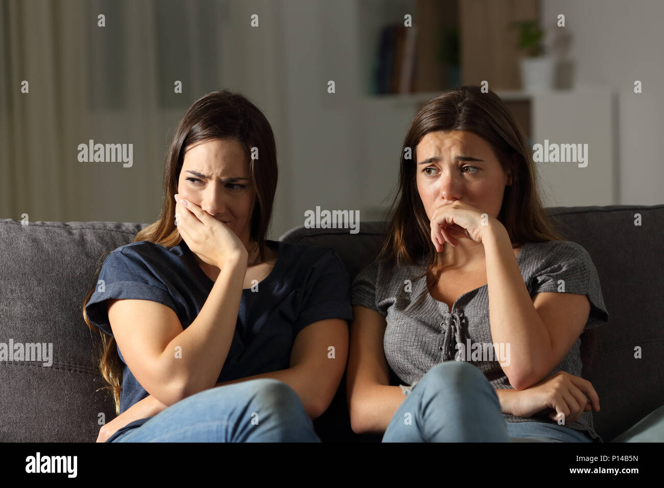Front view of two sad friends in the dark sitting on a couch in the ...