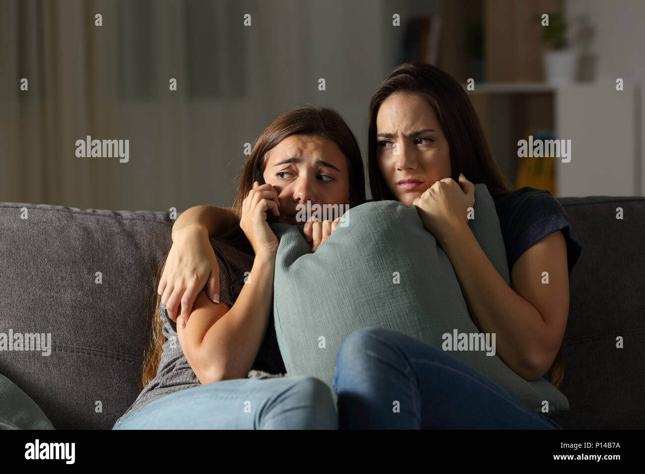 Scared friends at home calling police sitting on a couch in the living ...