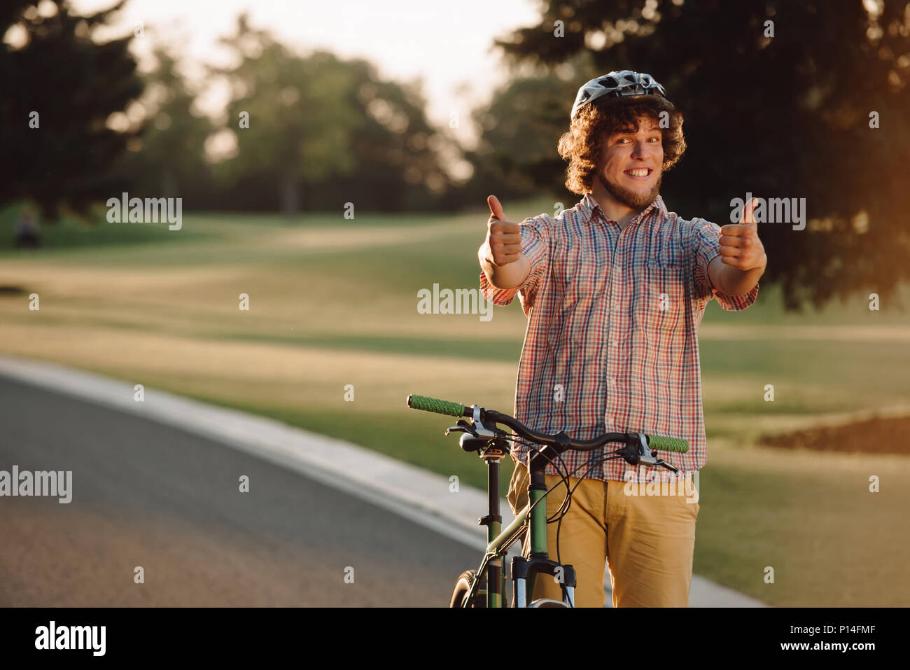Happy cyclist giving two thumbs up outdoors. Portrait of cheerful guy ...