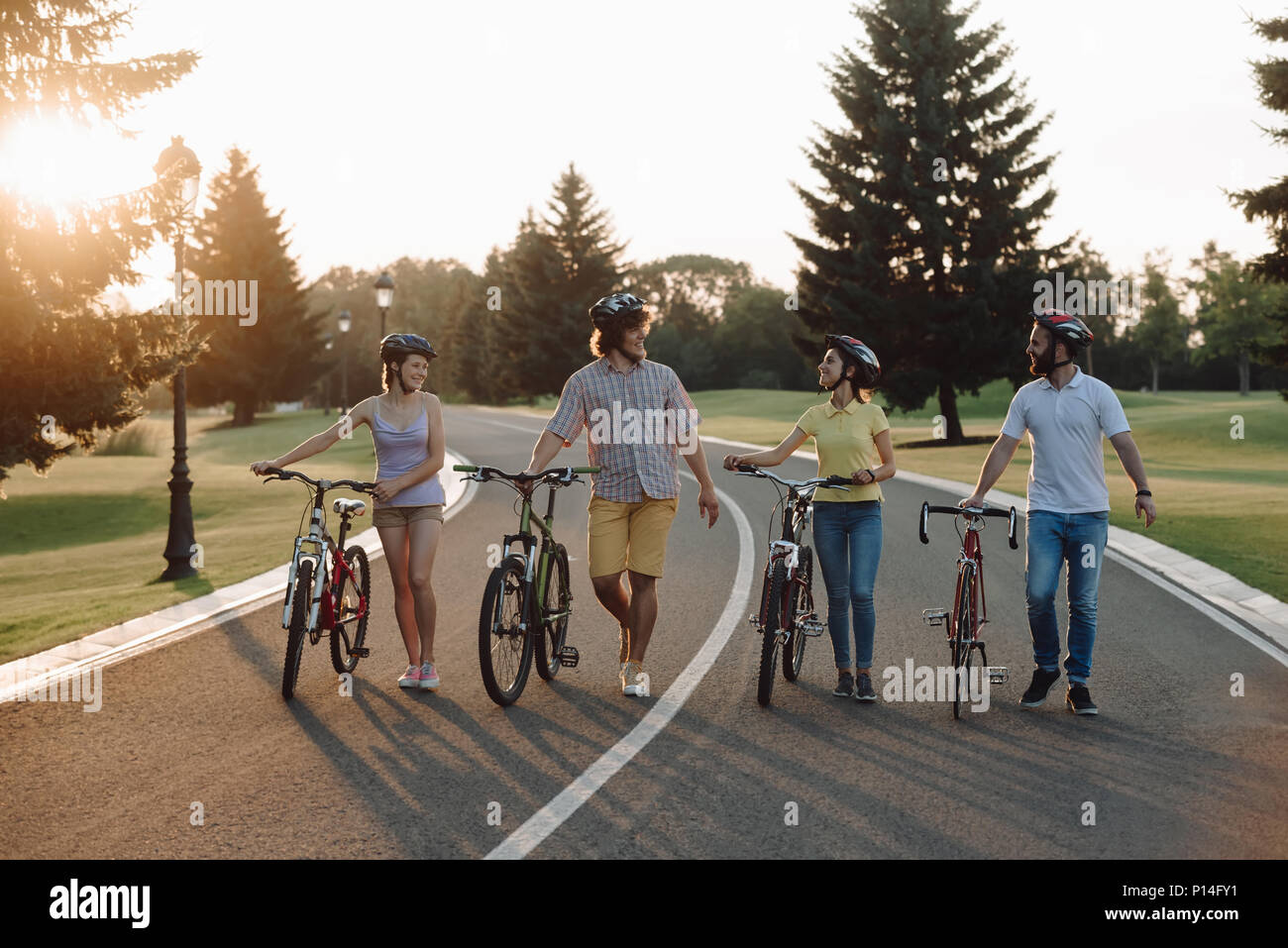 Group of cheerful cyclists walking with bicycles down the road. Four ...