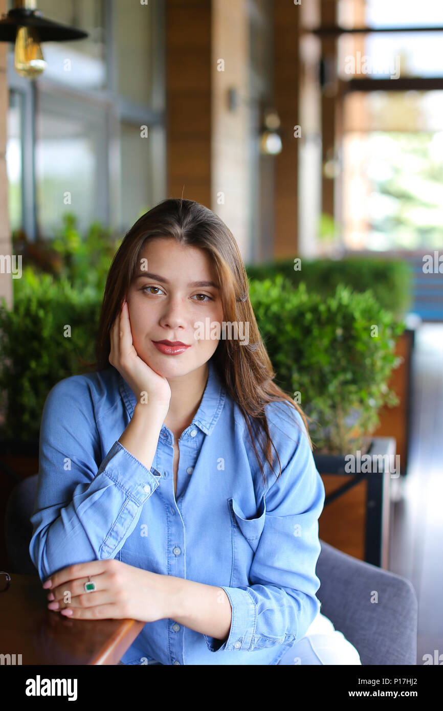 Girl sitting at cafe leaning on hand, wearing jeans shirt Stock Photo ...