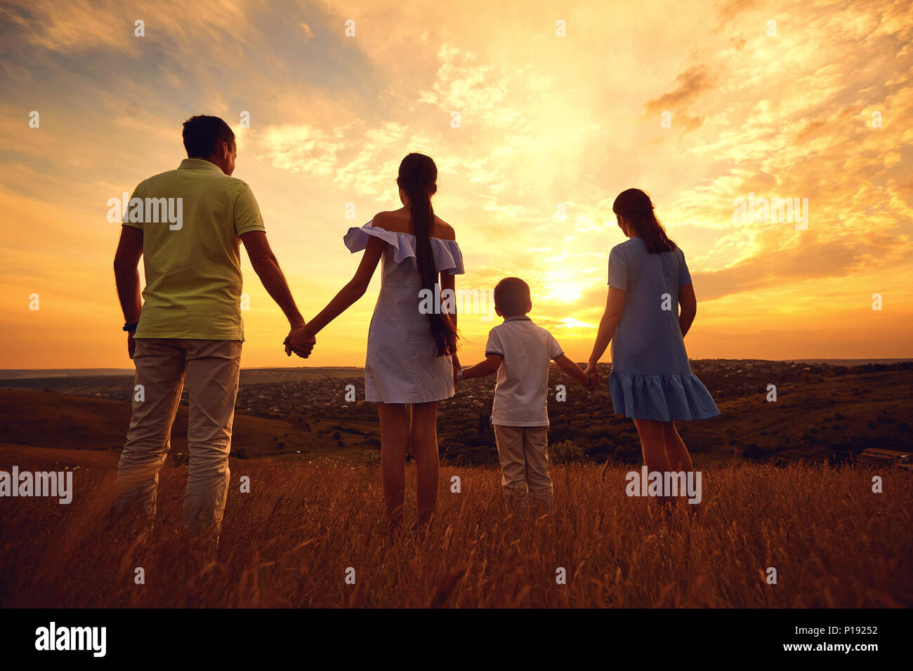 A happy family is standing in the nature at sunset in the evening. Back ...
