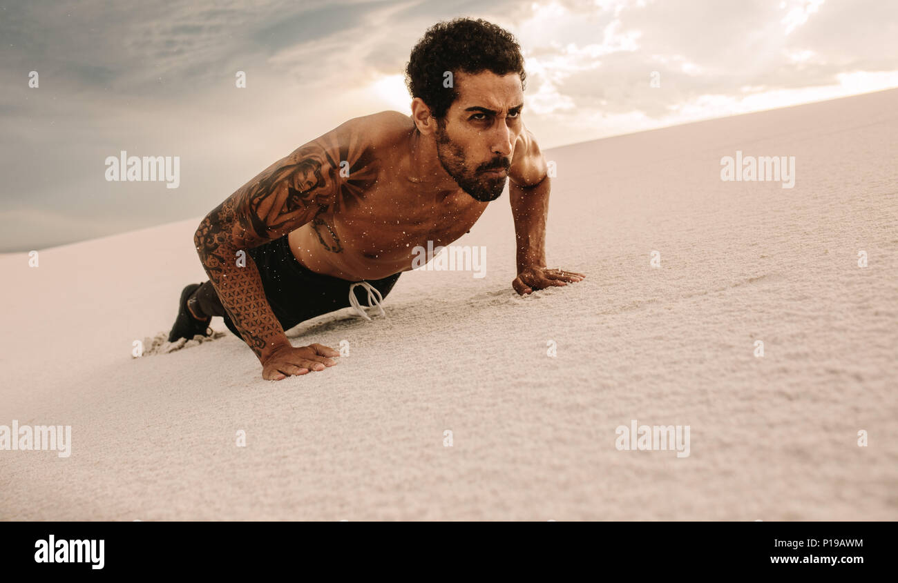Fit man doing push ups over sand dunes. Muscular man working out on ...