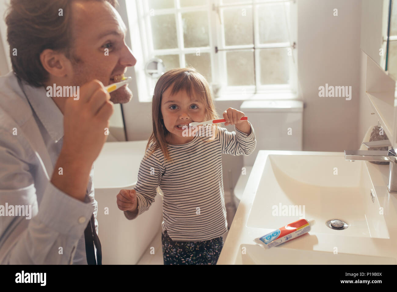 Father and daughter brushing teeth standing in bathroom. Man teaching ...