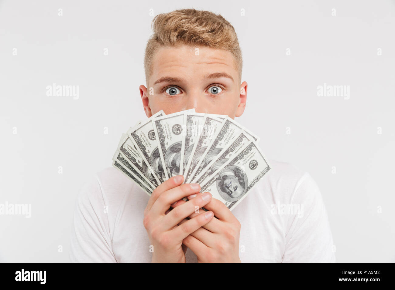 Portrait of an excited teenage boy holding money banknotes at his face ...