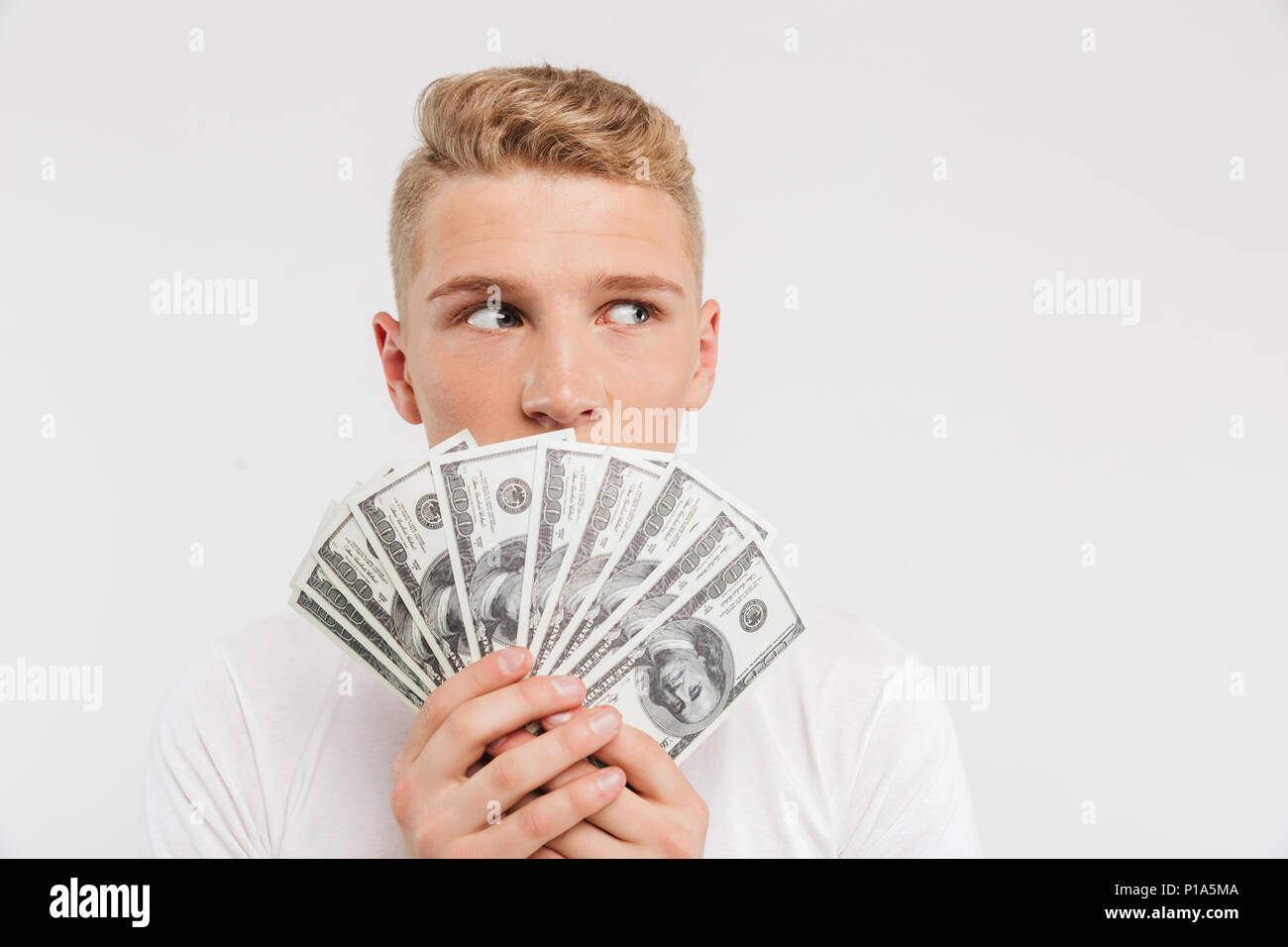 Portrait of a surprised teenage boy holding money banknotes at his face ...