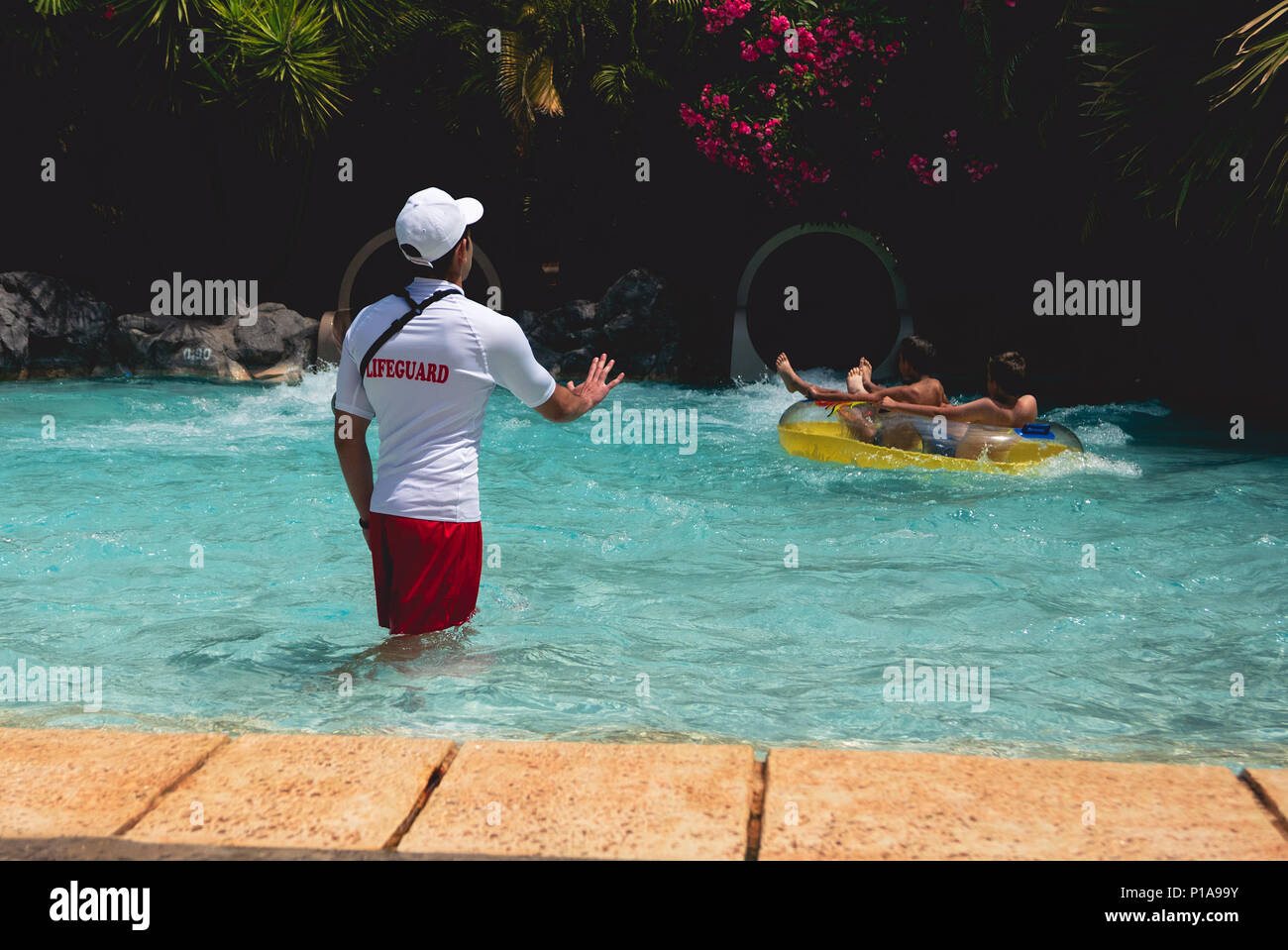 Back view on lifeguard who shows stop sign for kids floating on pontoon ...