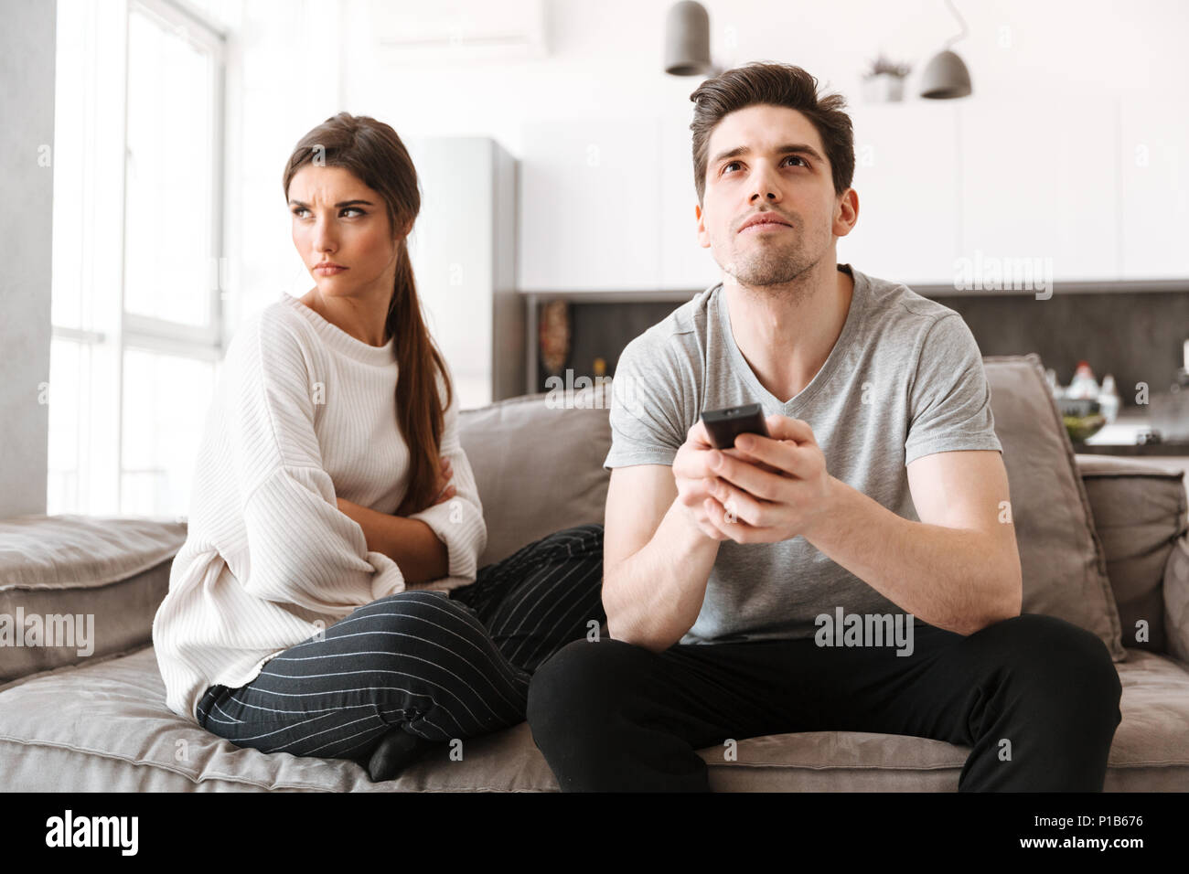 Portrait of an angry young woman sitting with her boyfriend on a couch ...