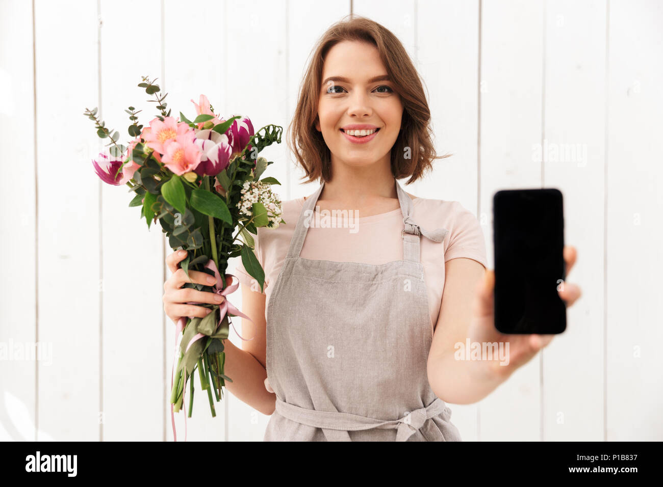Young cute happy florist woman standing with flowers in workshop ...