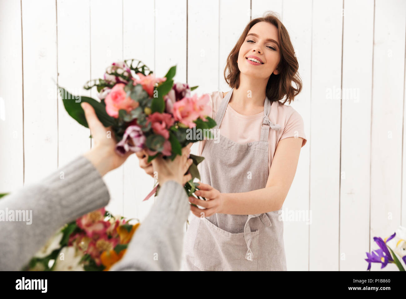 Young cute florist lady standing with flowers in workshop with buyer ...