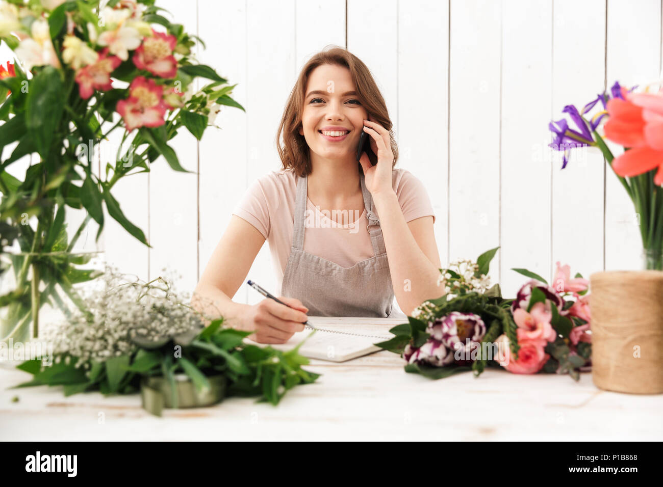 Young cute happy florist lady over flowers in workshop talking by ...