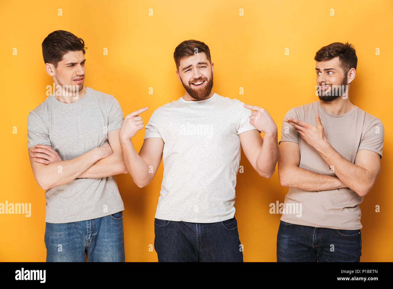 Two young confused men looking at their male friend isolated over ...