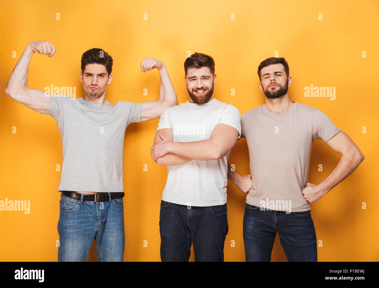 Three young confident men looking at camera isolated over yellow ...