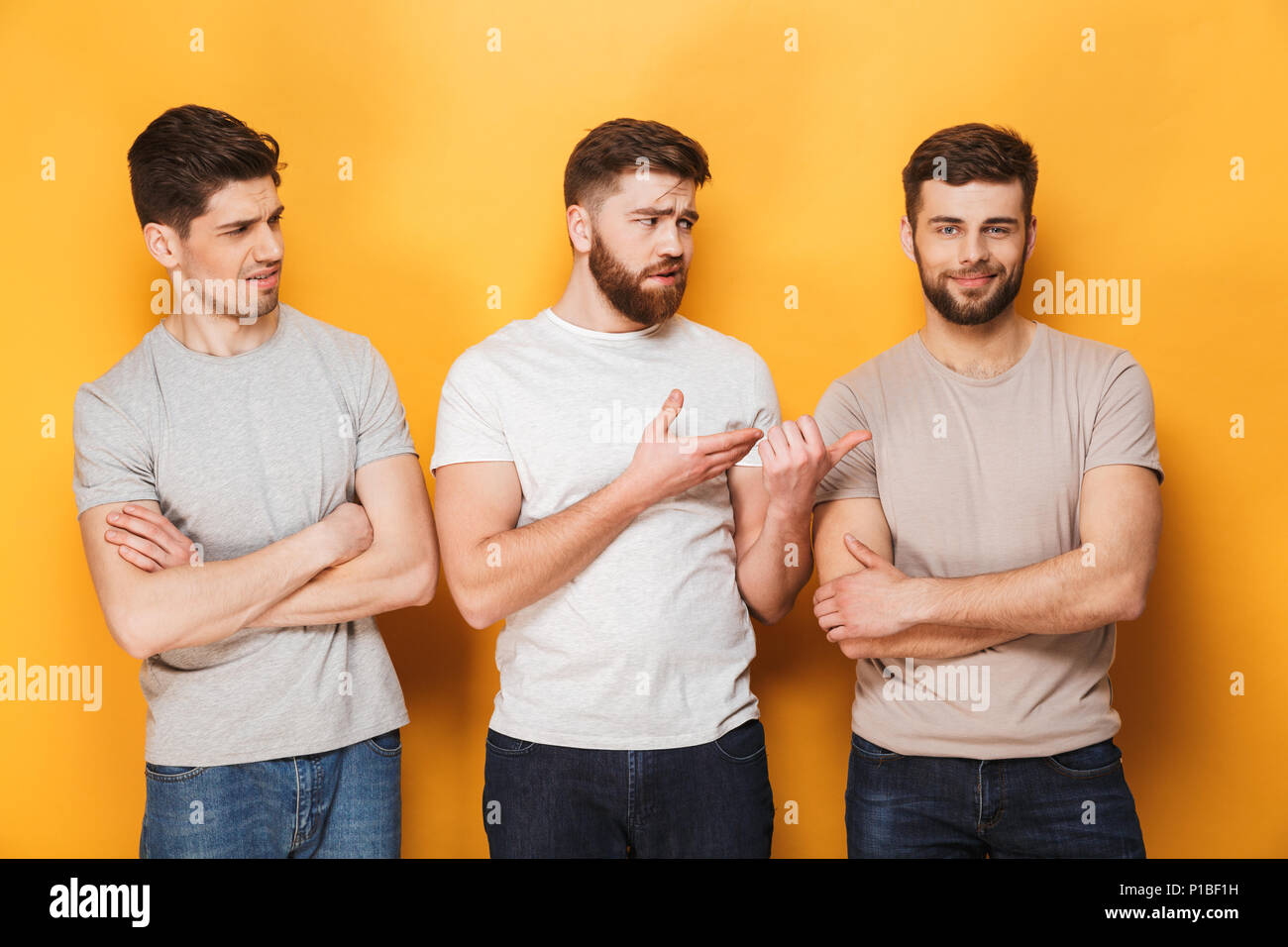 Two young upset men looking at their male friend isolated over yellow ...