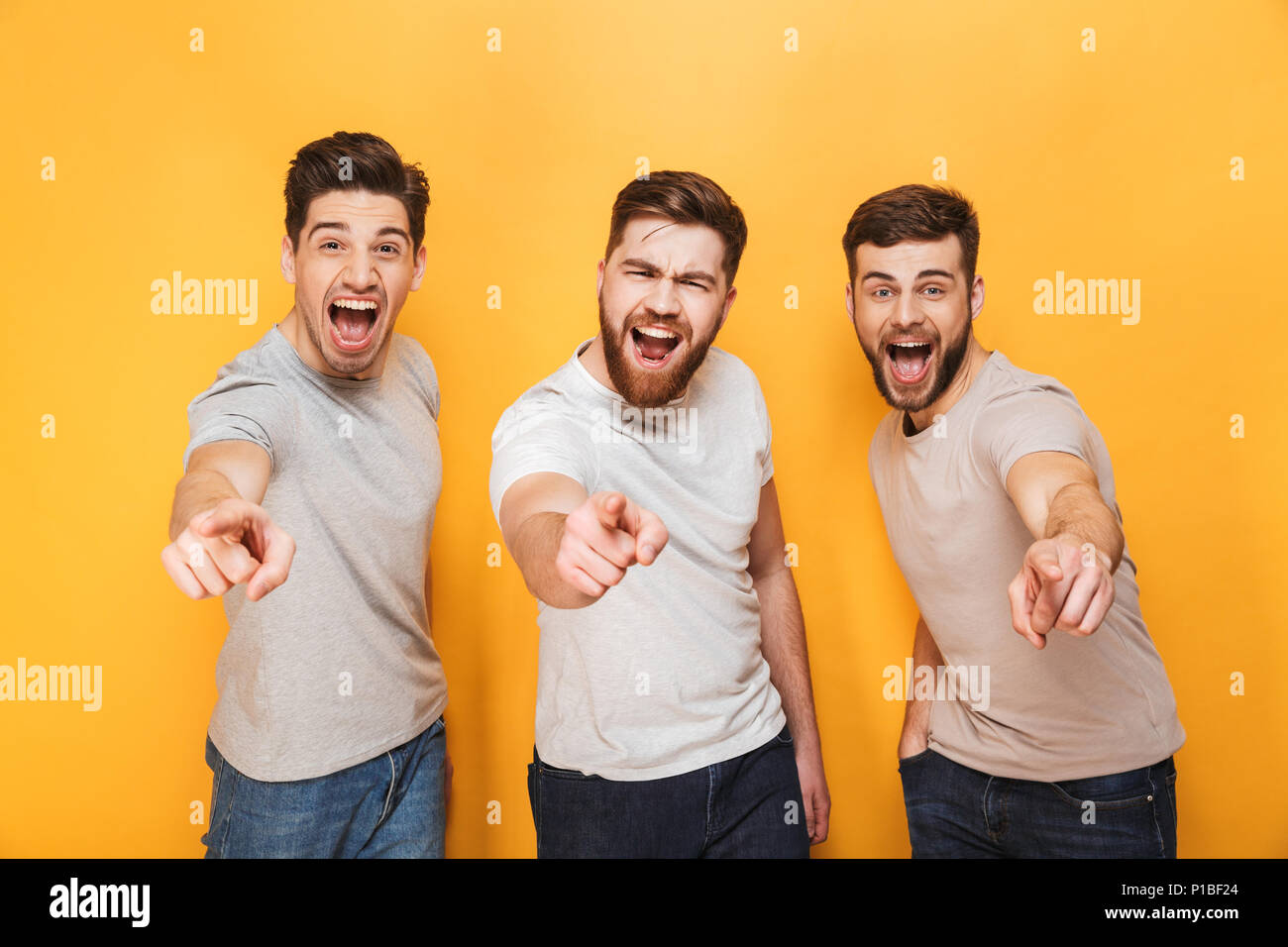Three young excited men pointing at camera and screaming isolated over ...