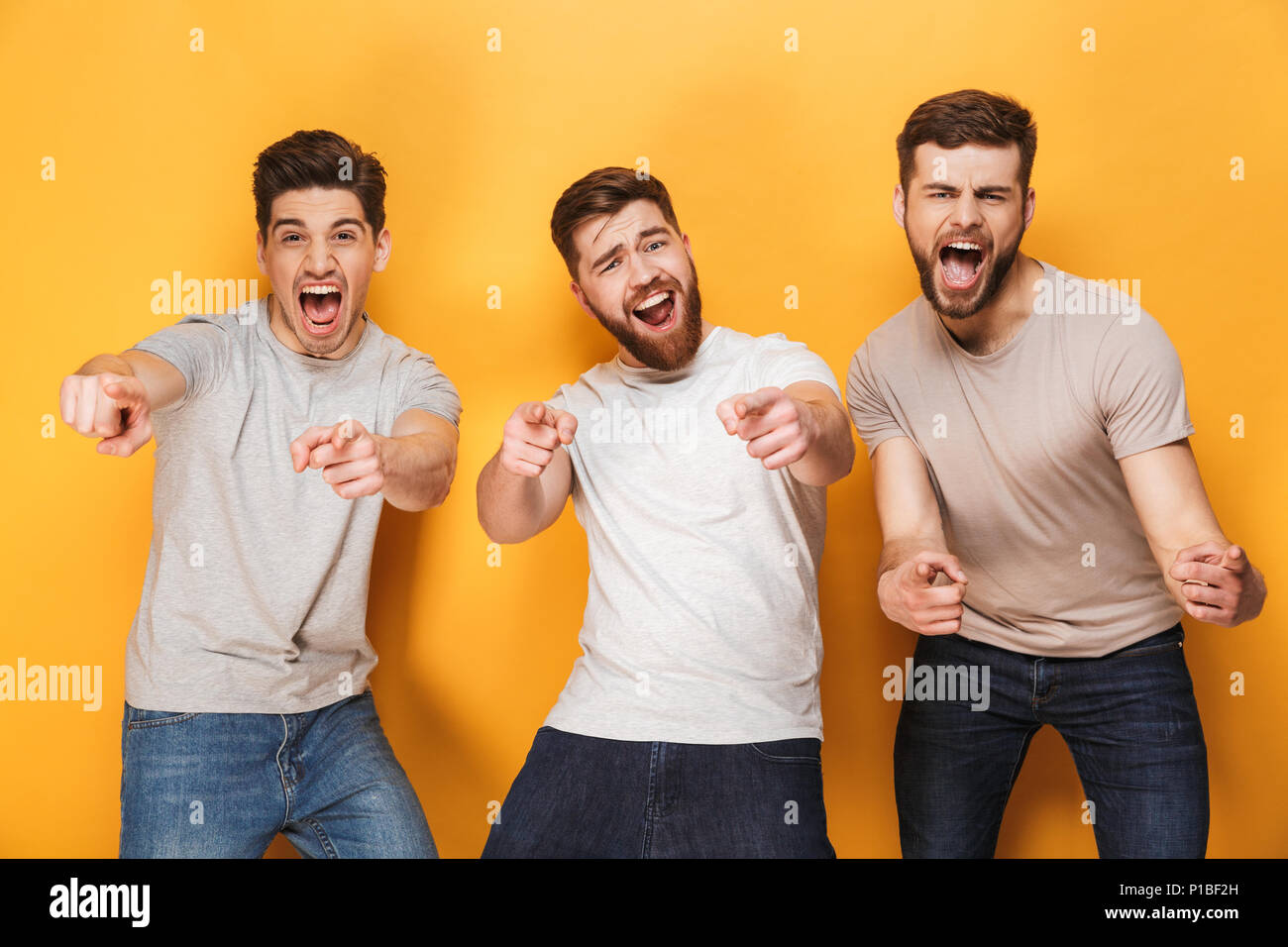 Three young happy men pointing at camera and screaming isolated over ...