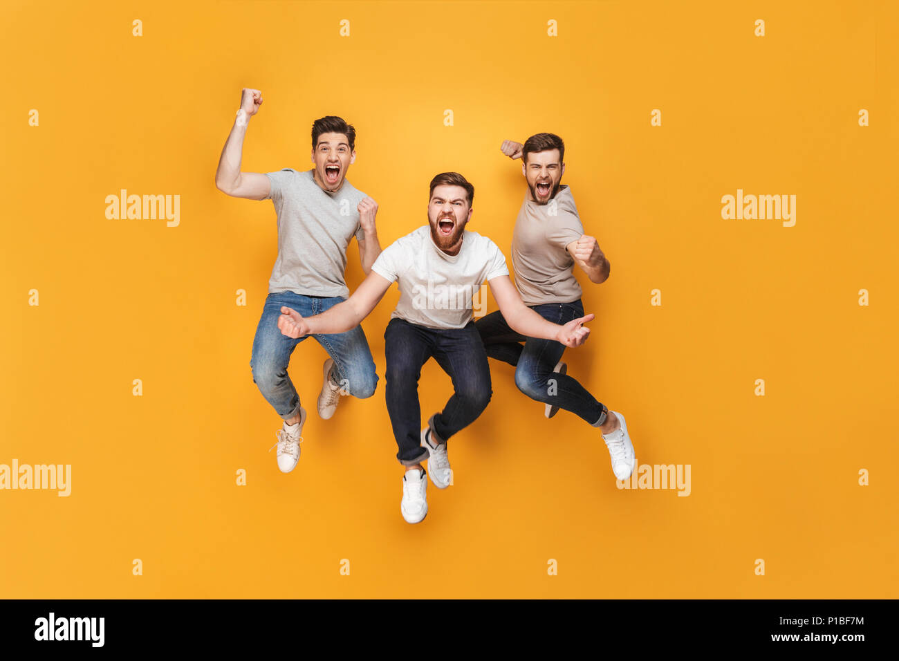 Three young happy men jumping together isolated over yellow background ...