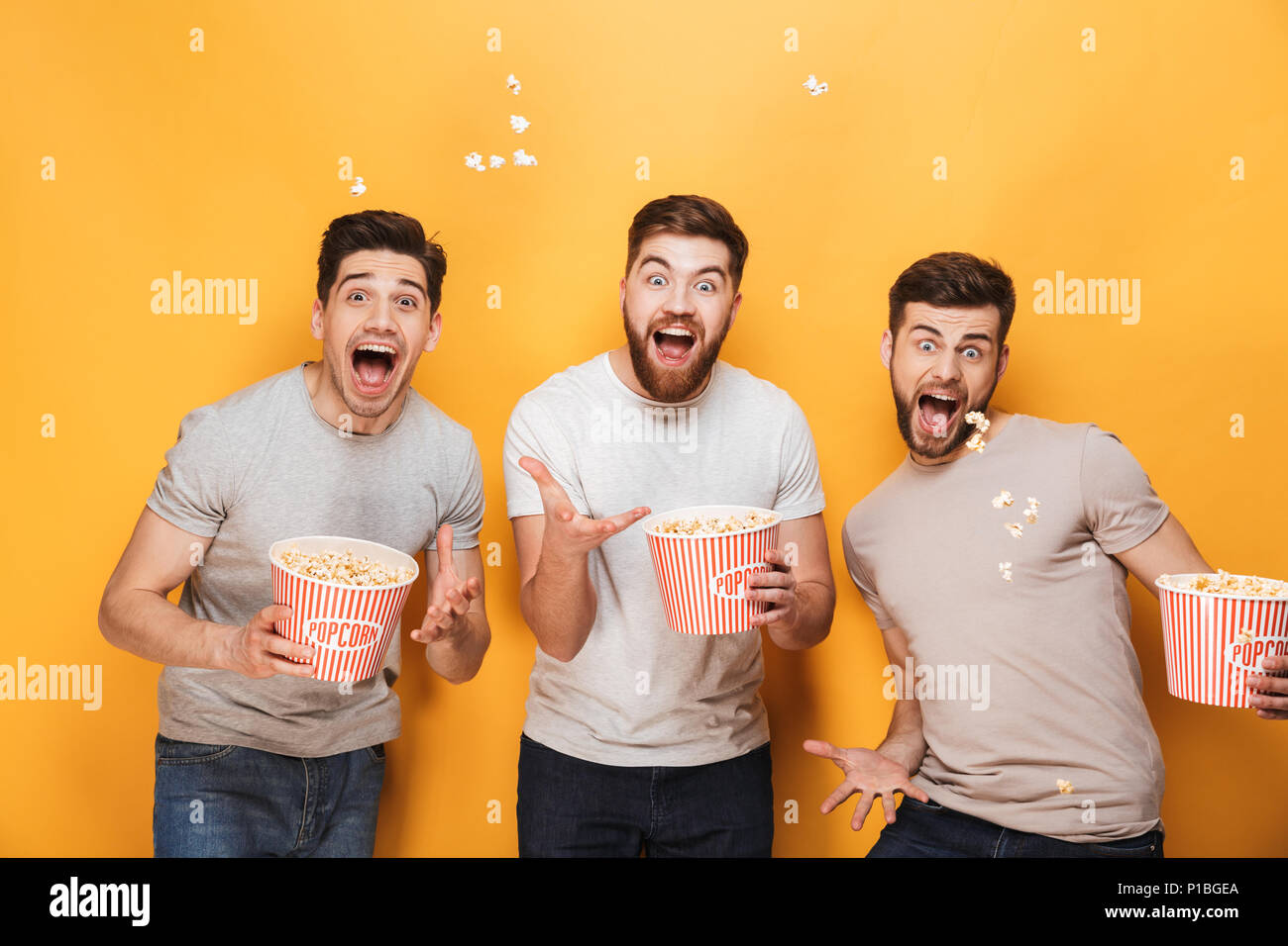 Three young excited men eating popcorn and celebrating isolated over ...