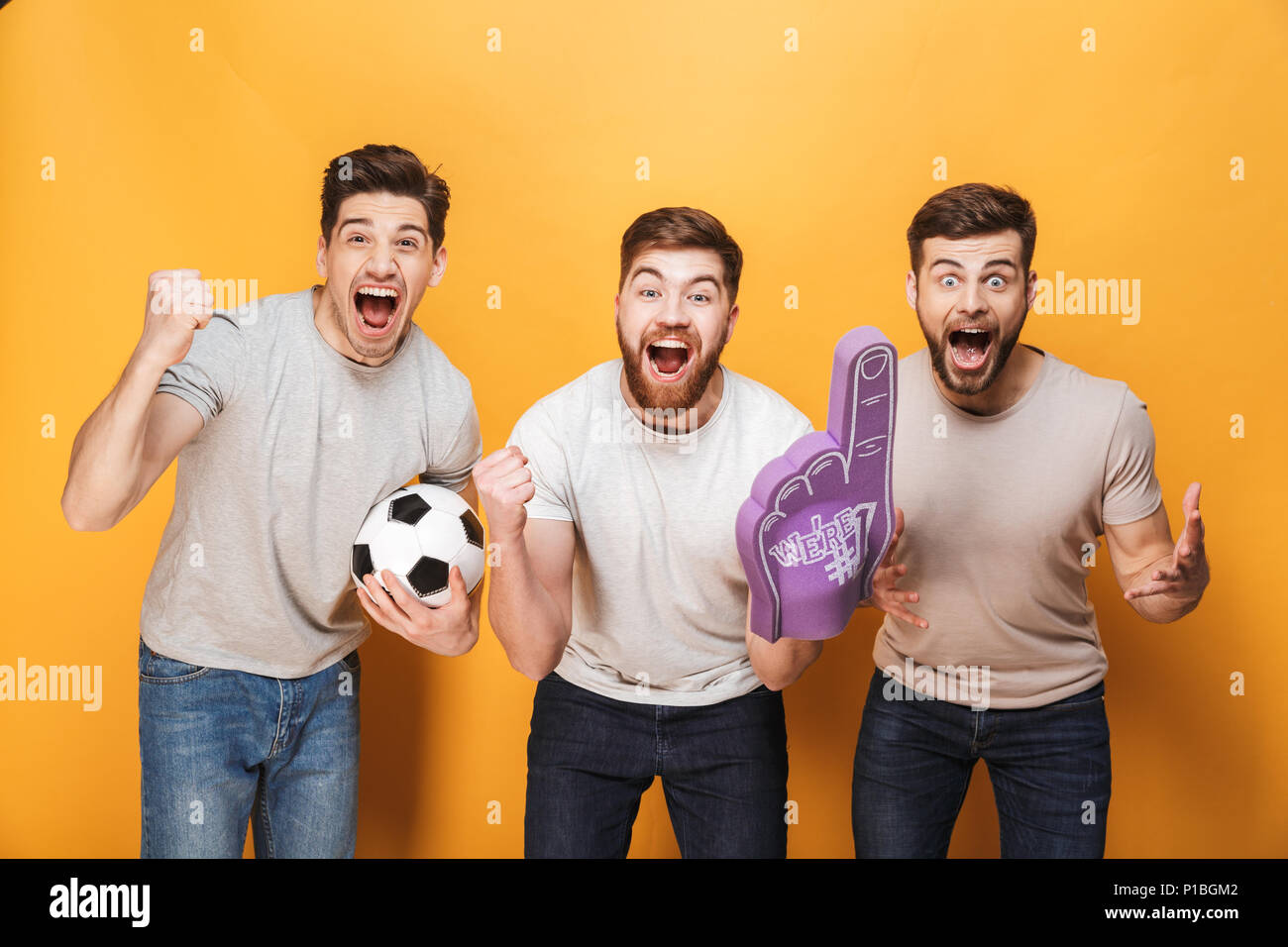 Three young cheery men football fans celebrating isolated over yellow ...