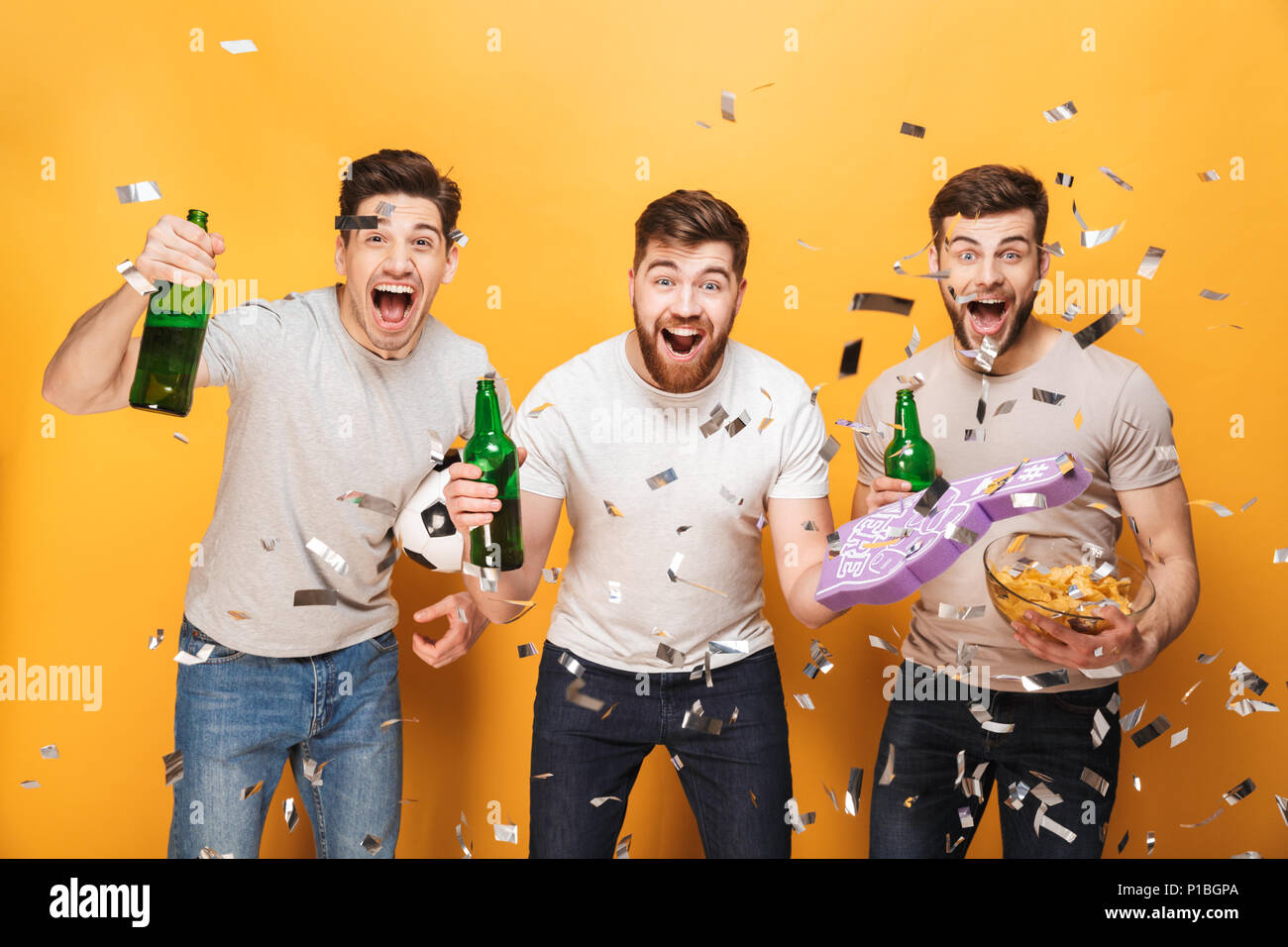 Three young joyful men football fans celebrating with beer and snacks ...